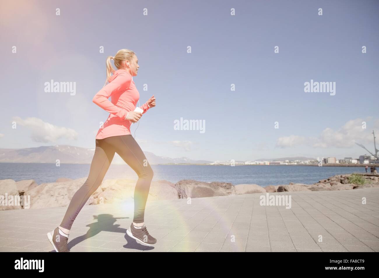 Side view of teenage girl wearing sports clothes jogging by water ...
