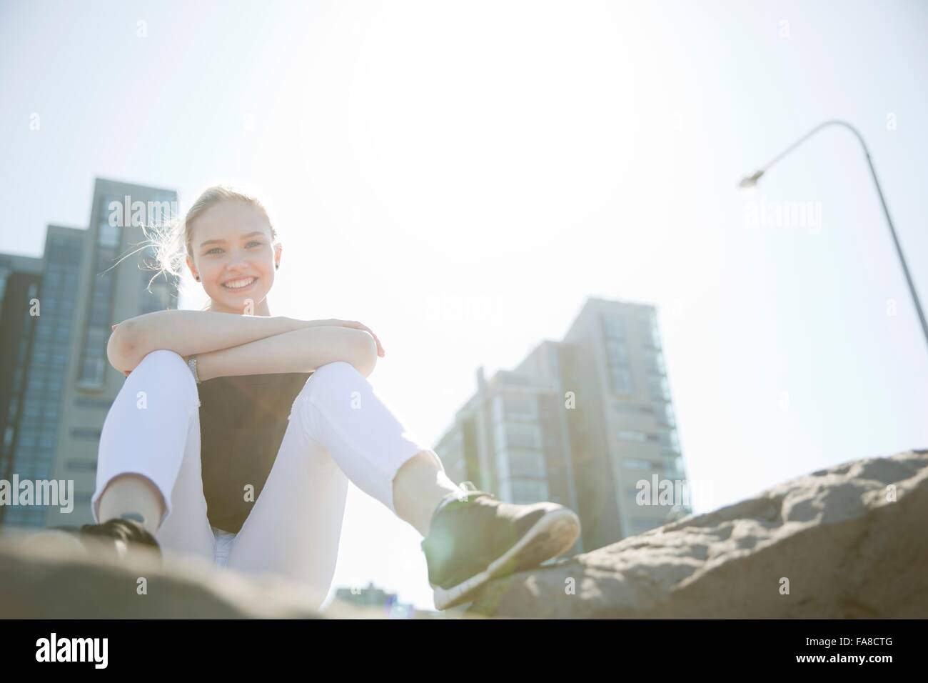 Low angle view of high rise buildings and teenage girl sitting on rocks ...
