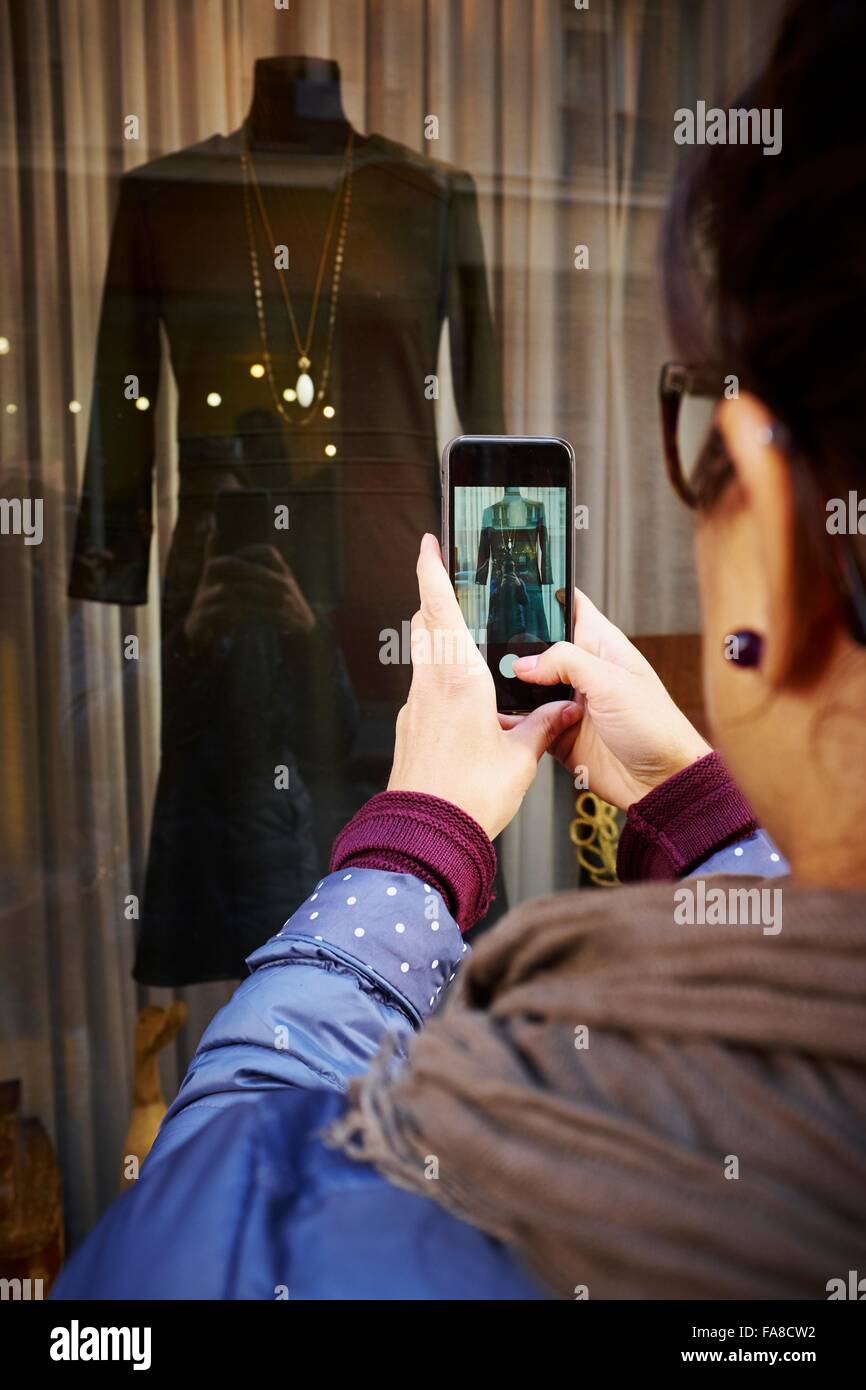 Mid adult woman photographing dress in shop window on smartphone Stock ...