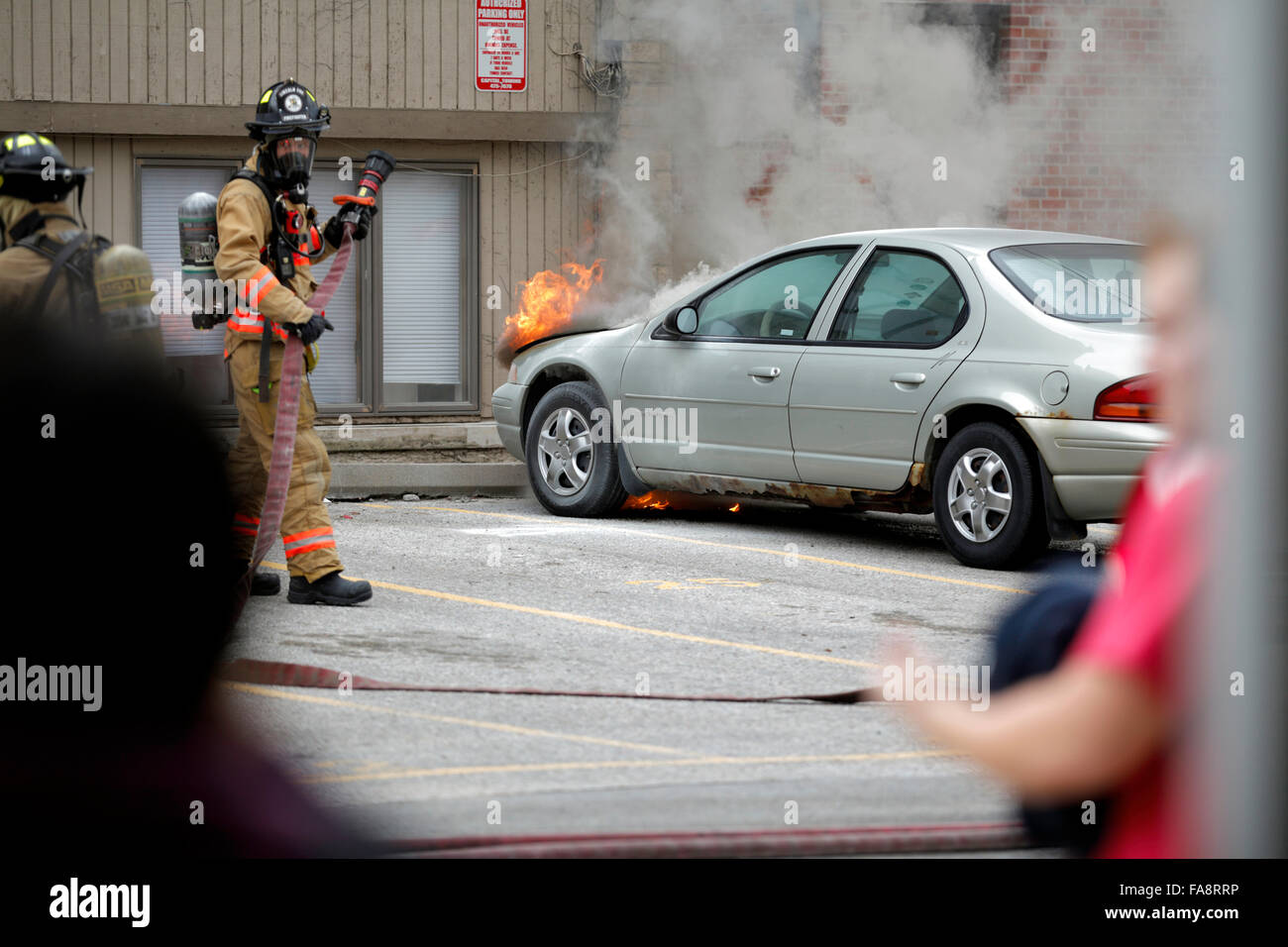 A firefighter prepares to extinguish a car fire as onlookers watch ...