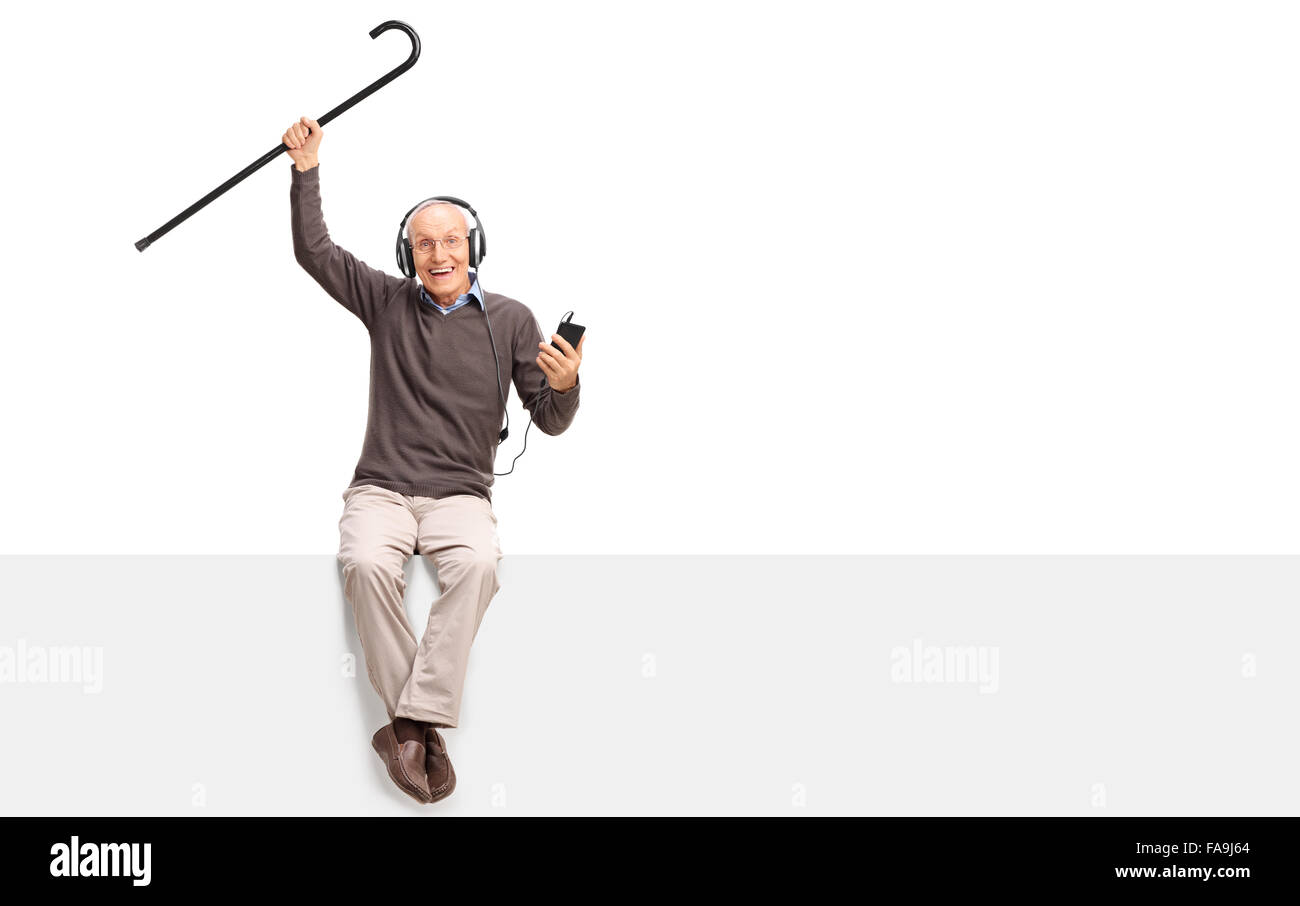 Senior man listening to music on headphones and lifting his cane in the ...