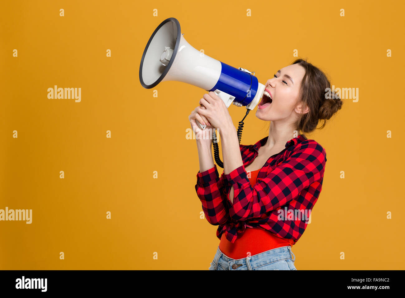Funny excited young woman in checkered shirt shouting in megaphone over ...