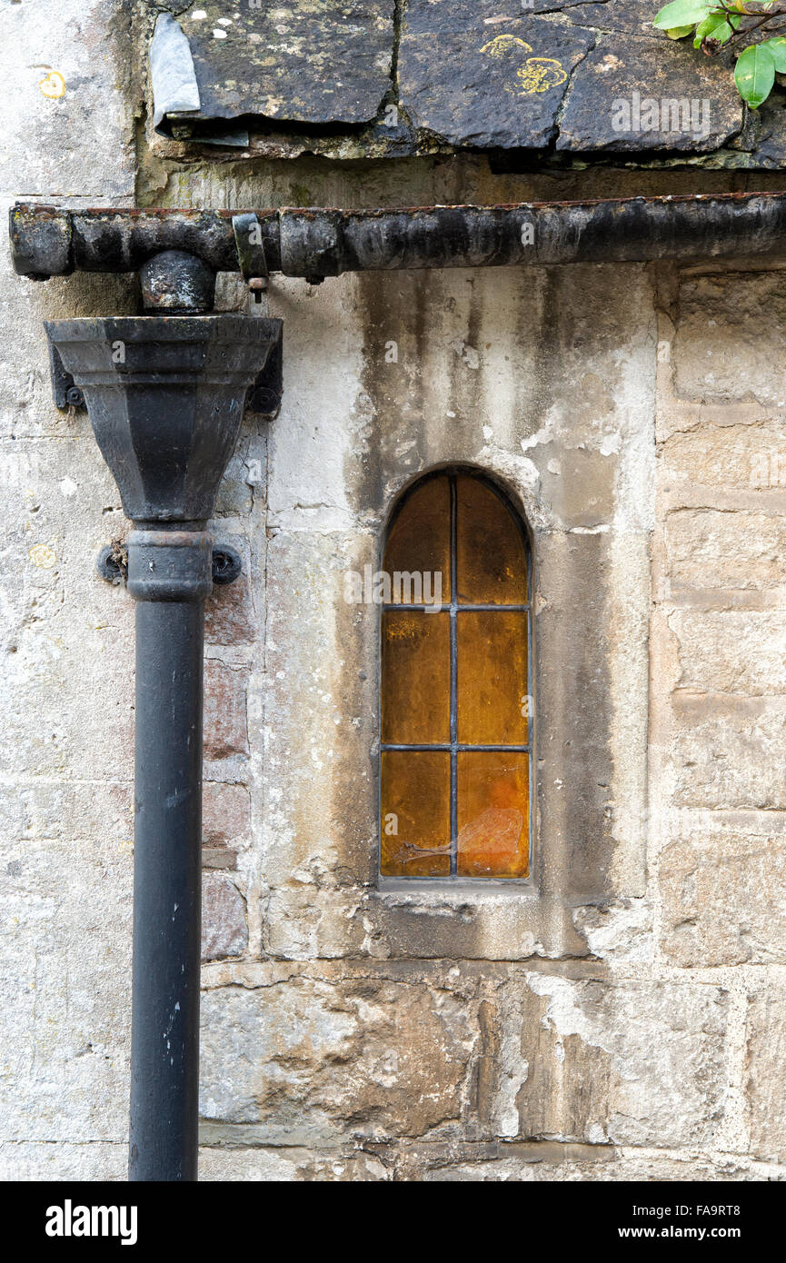 Small arched leaded yellow window and old guttering on a traditional ...