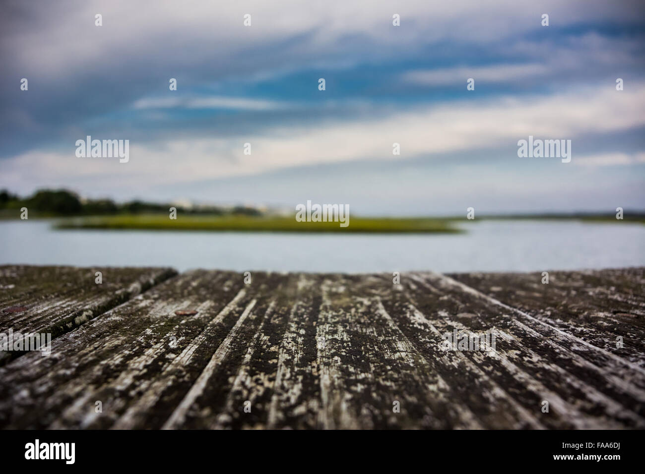 A sharp focus on a wooden boardwalk in front of a blurred marsh inlet ...