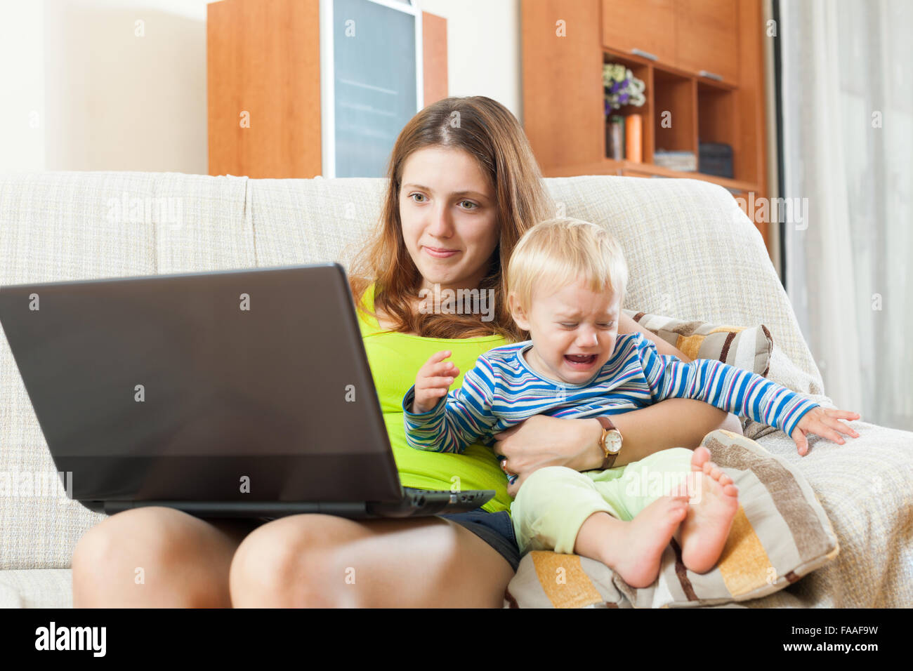 Whiner young mother with a crying baby, working with a computer at home ...