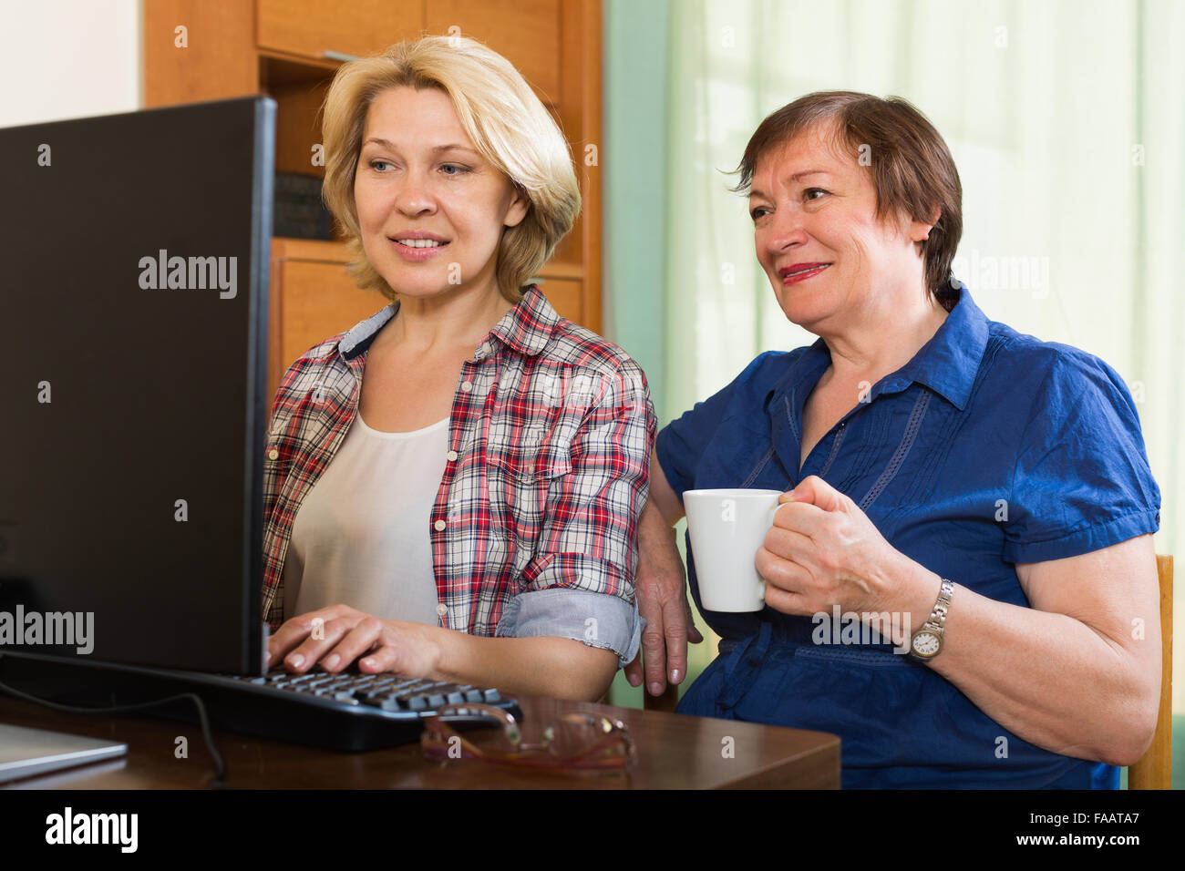 Two elderly women sitting in front of PC with coffee and laughing Stock ...