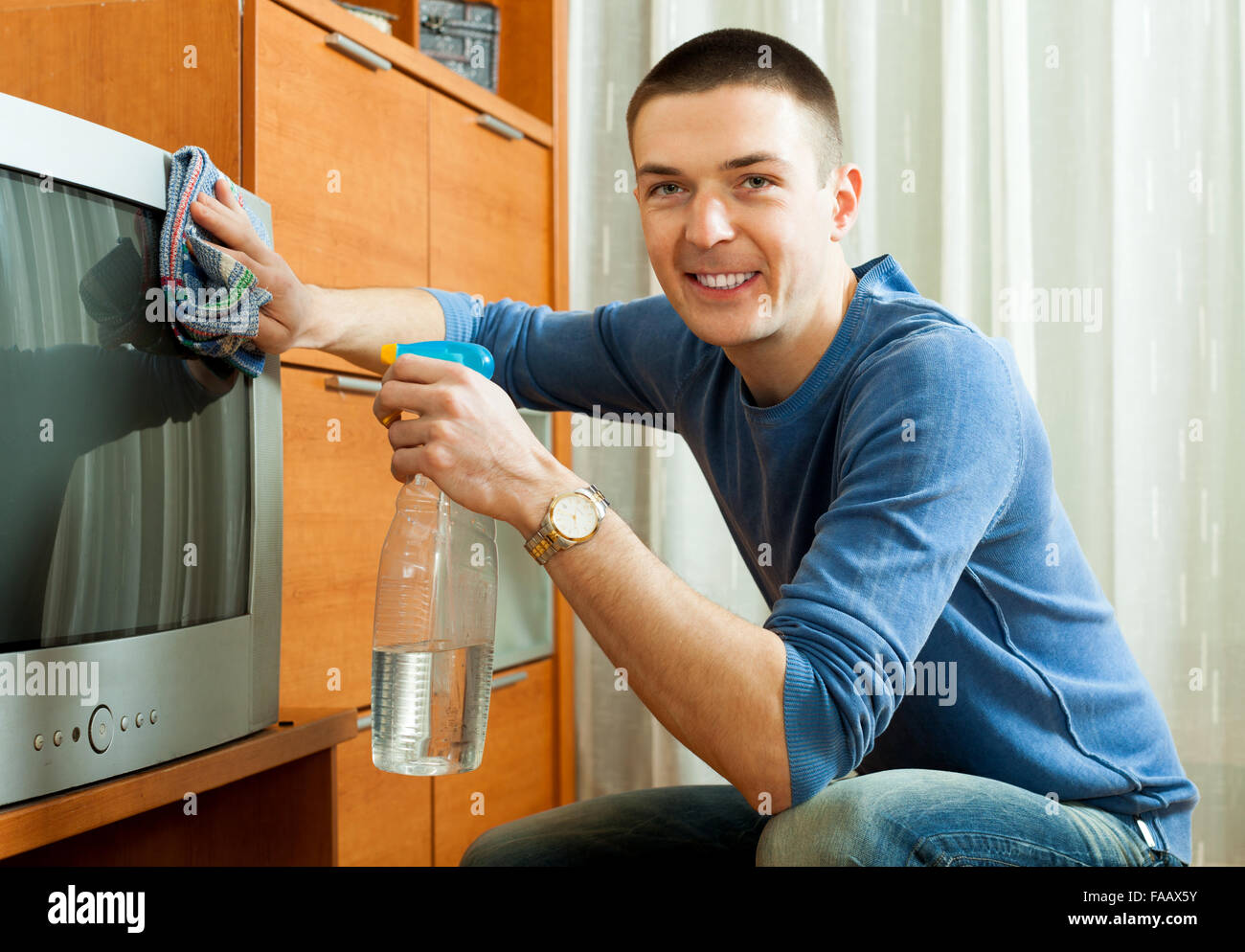Smiling guy in home cleaning TV at living room in home Stock Photo - Alamy