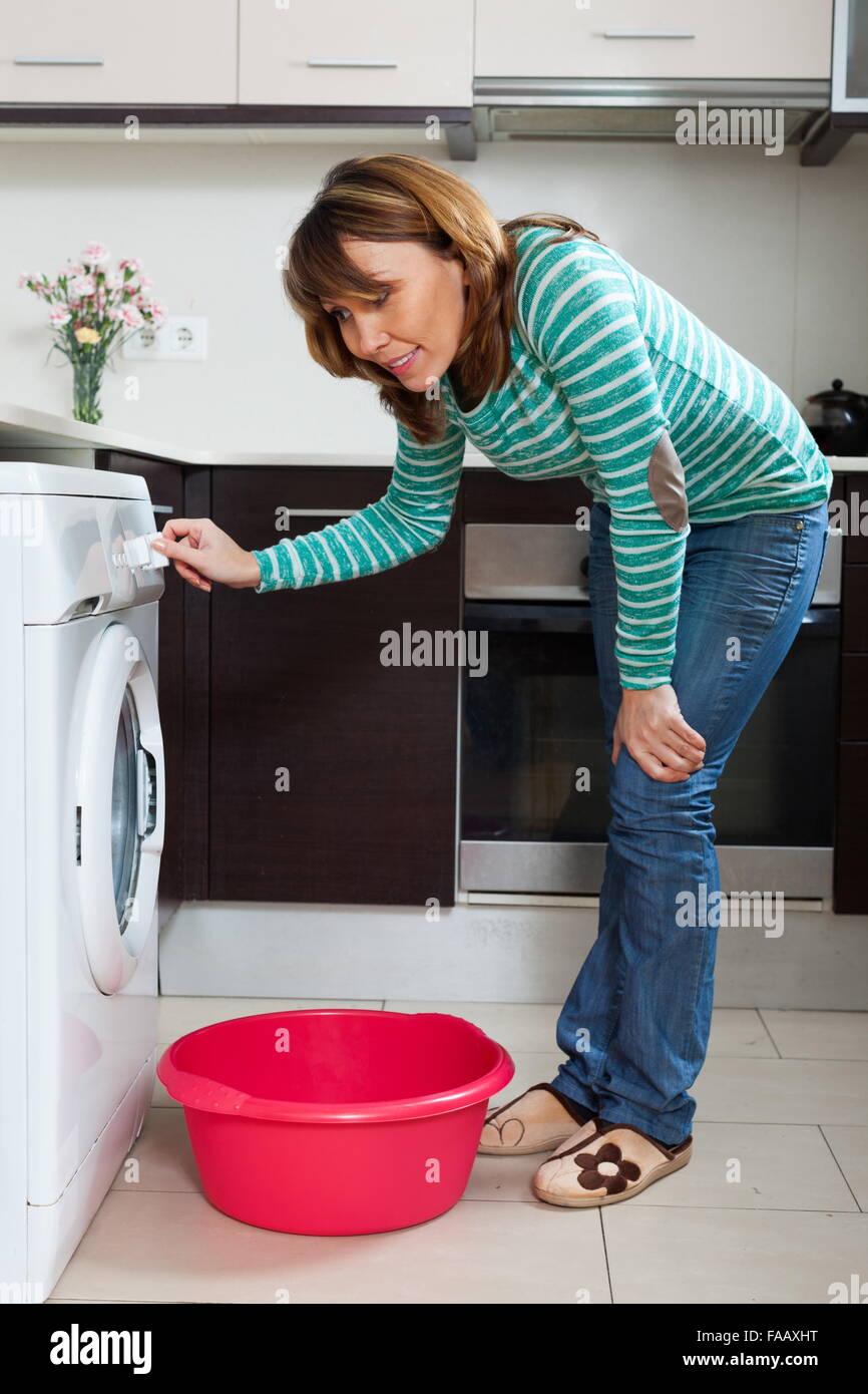 Ordinary woman in green doing laundry with washing machine at home ...