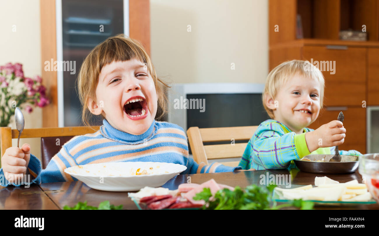 Two happy children eating food at table Stock Photo - Alamy
