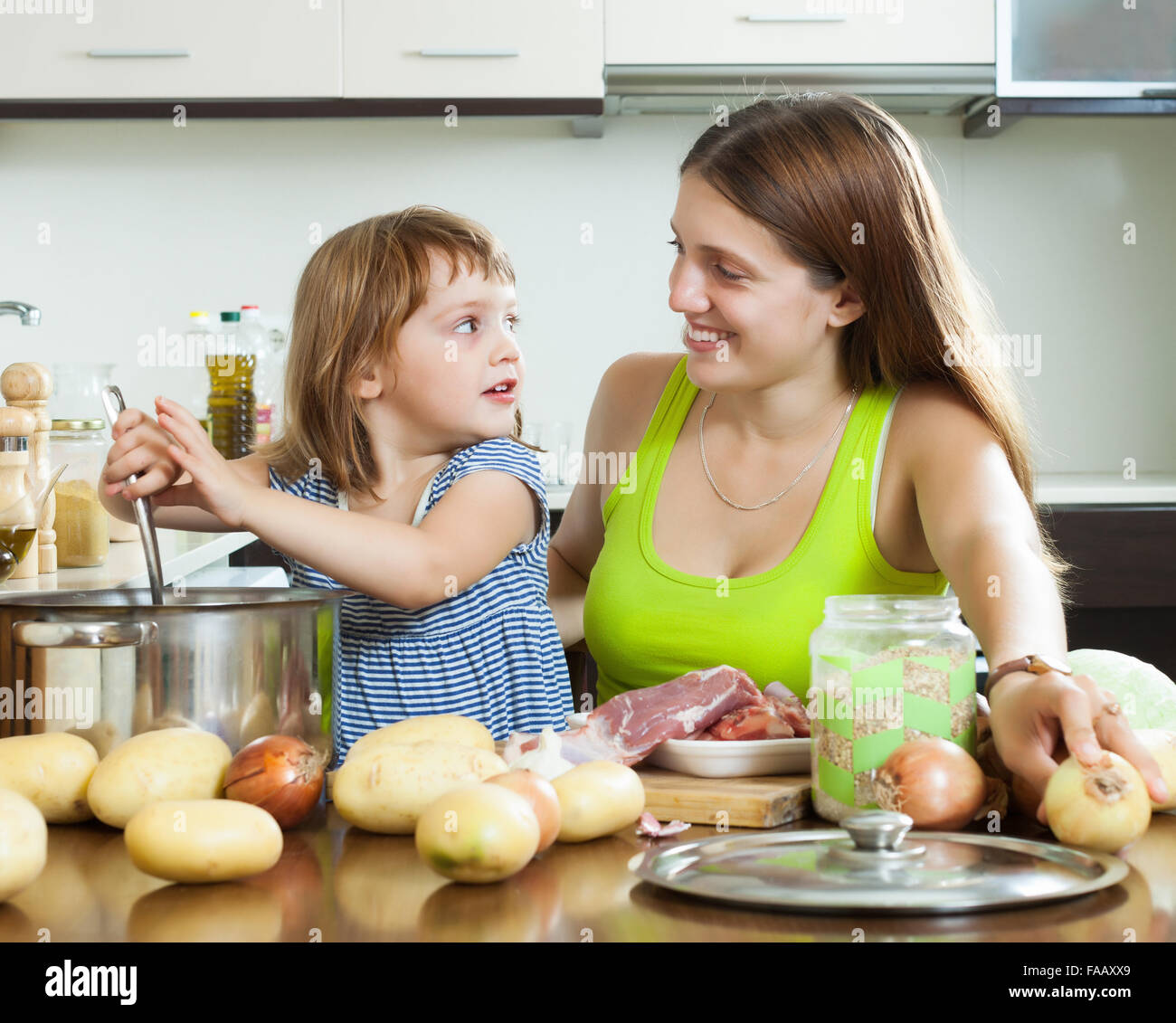 Happy mother with child cooking soup from meat and vegetables at ...