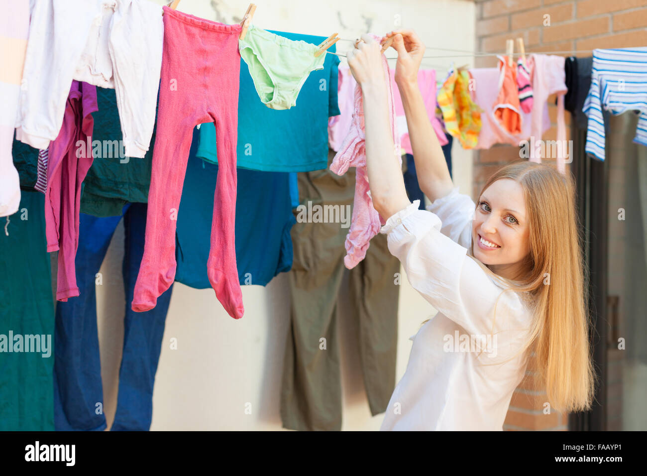 Positive long-haired girl drying clothes on clothes-line after laundry ...