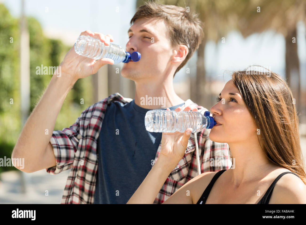 Thirsty young male with girlfriend drinking water from bottle at sunny ...