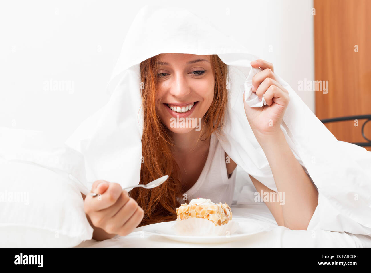 Happy young woman eating sweet cake under sheet in bed Stock Photo - Alamy