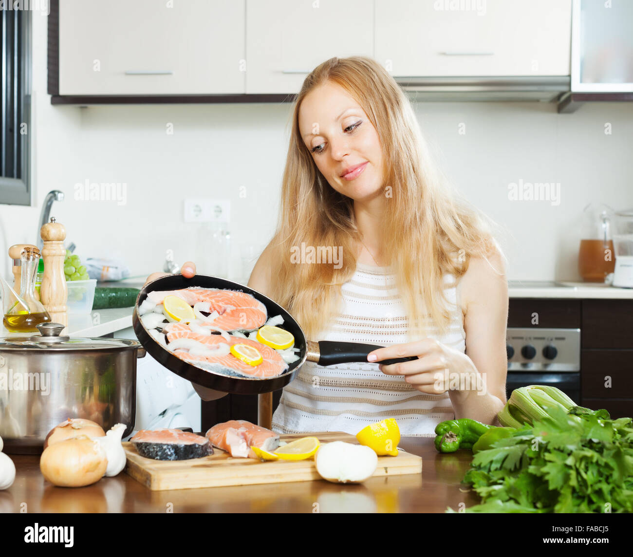 Smiling woman cooking salmon fish with lemon on griddle at kitchen ...