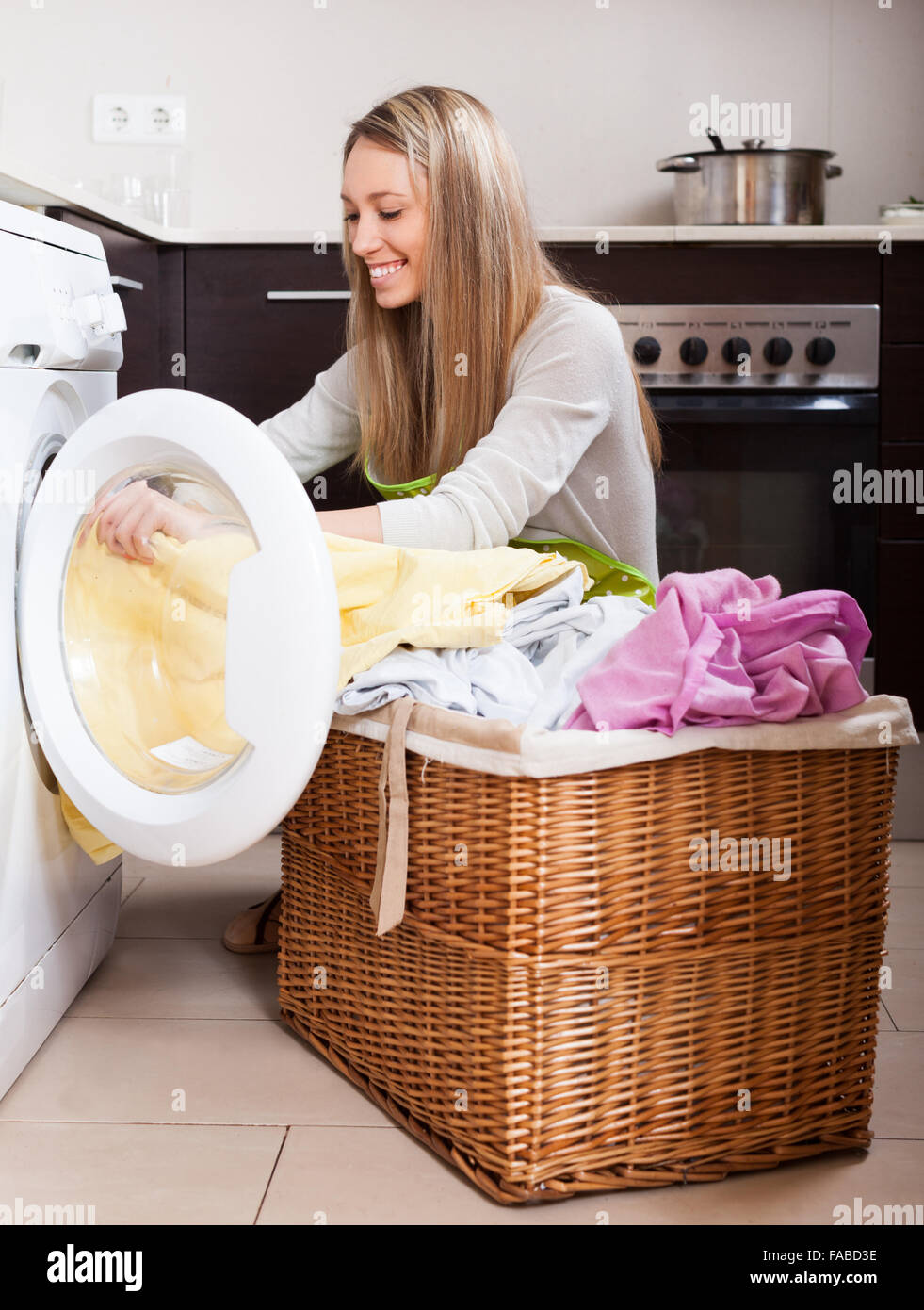 Home laundry. Happy blonde woman loading clothes into washing machine ...