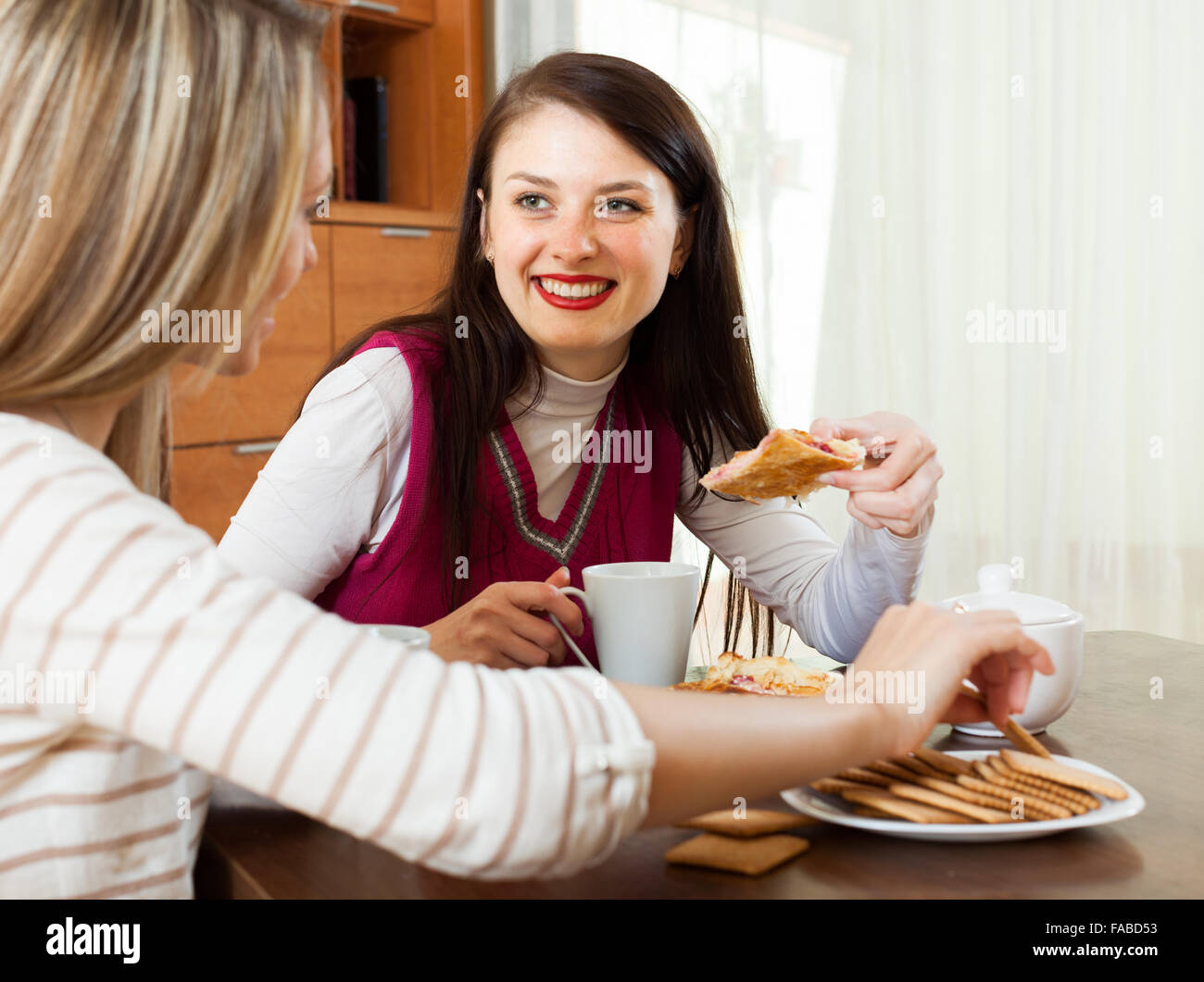 two happy young women sitting at table, gossiping and drinking tea in ...
