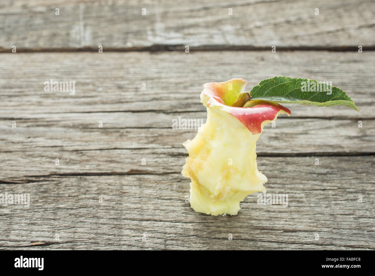 Bitten into apple core with green leaf on rustic wood Stock Photo - Alamy