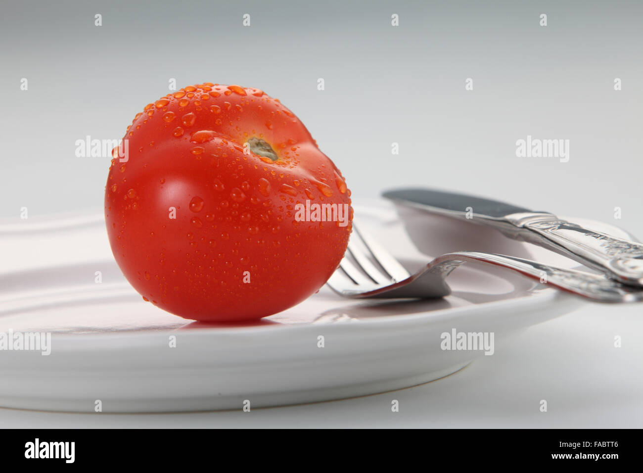 fresh tomato on the plate with cutlery Stock Photo - Alamy