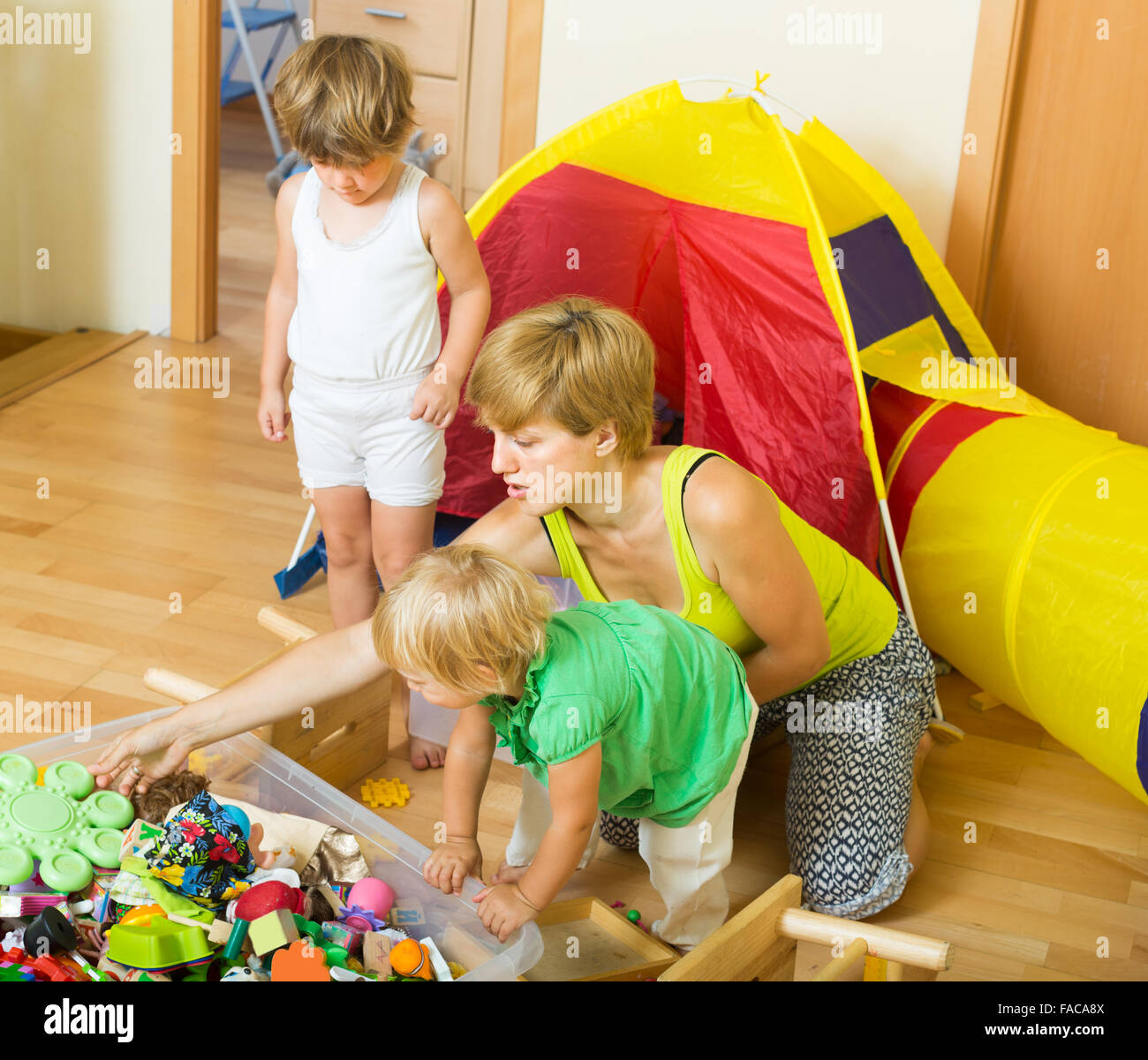 Two little girls and mother collecting toys in plastic box Stock Photo ...