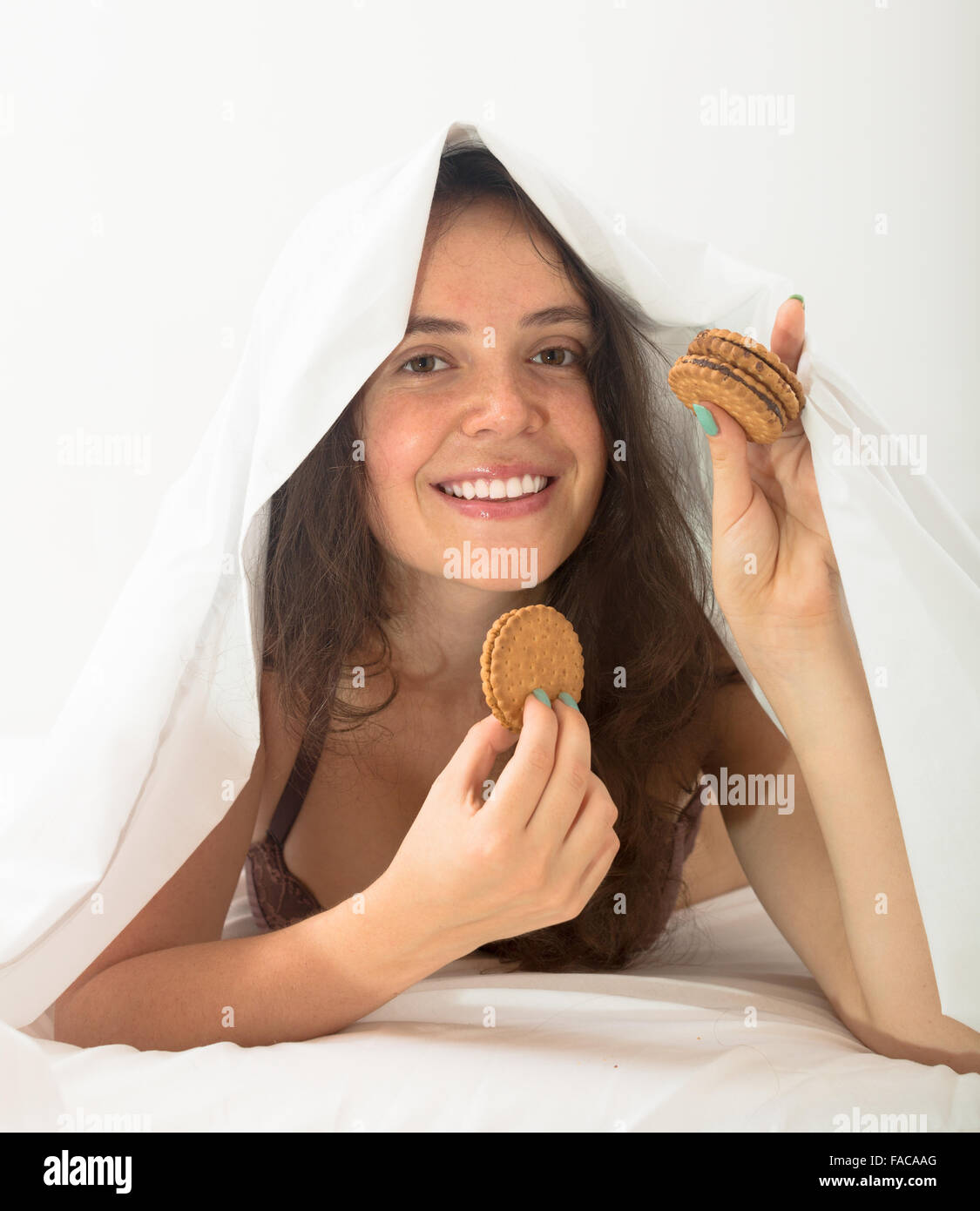 Happy young woman eating chocolate chip cookies in her bed and smiling ...