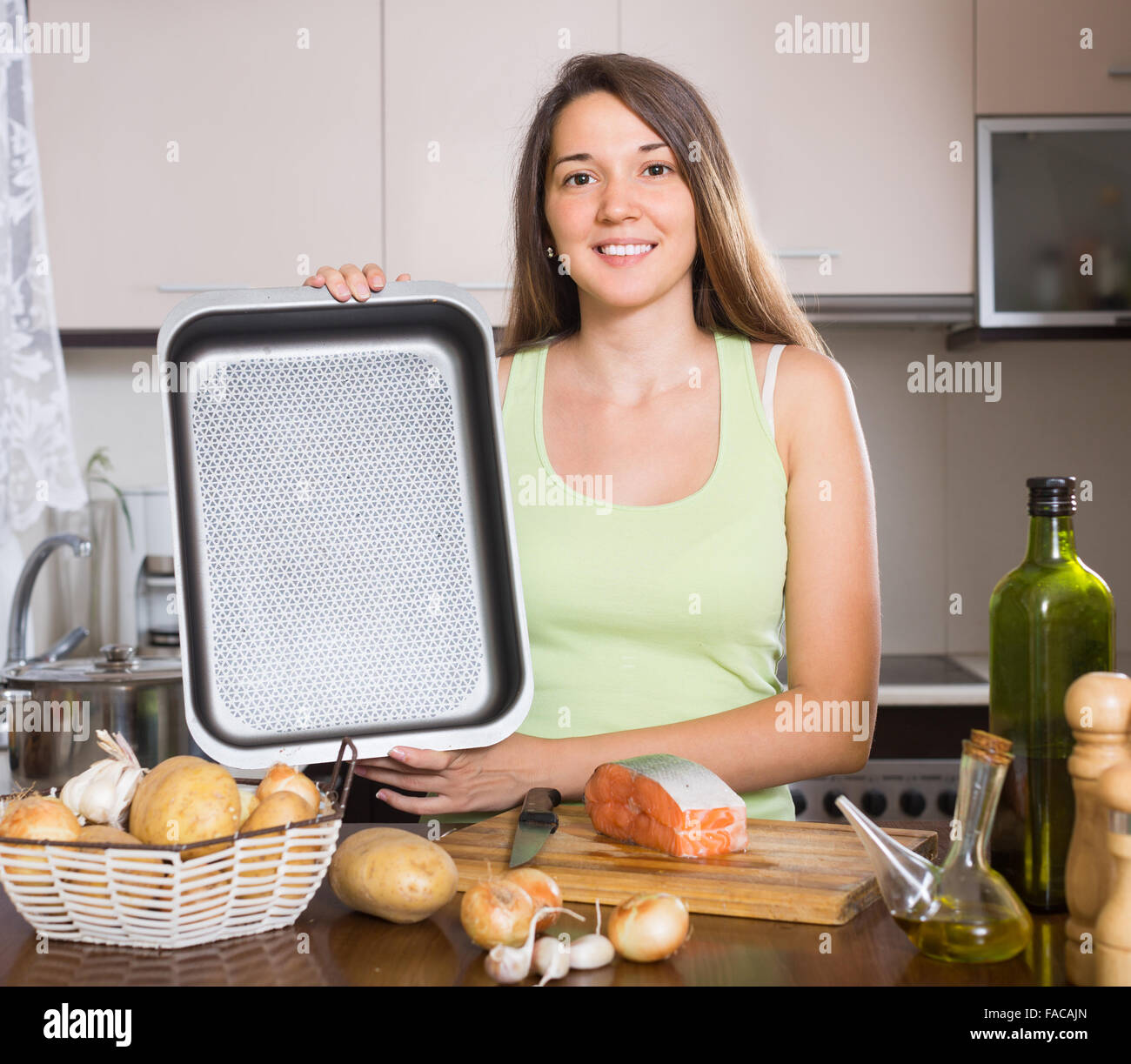 Smiling young woman cooking salmon fish in frying pan at kitchen Stock ...