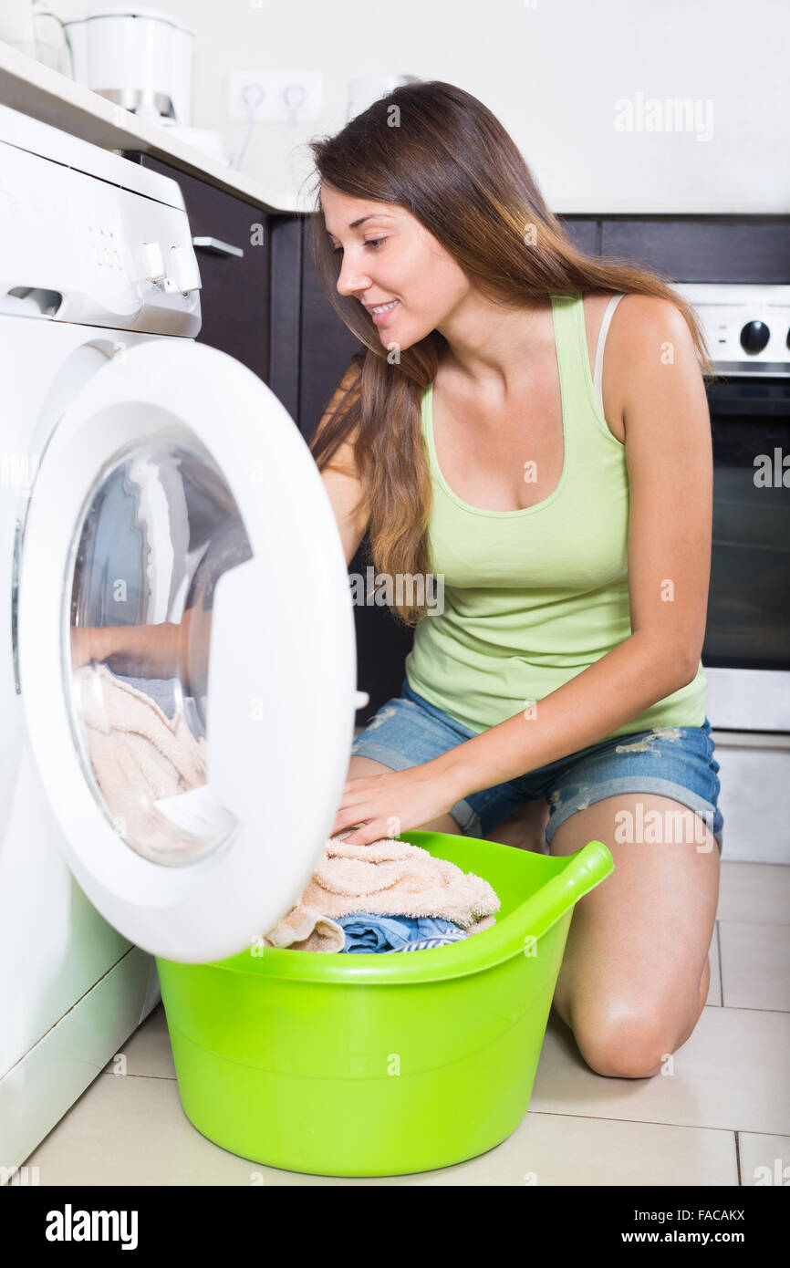 Home laundry. Happy young girl loading clothes into washing machine in ...