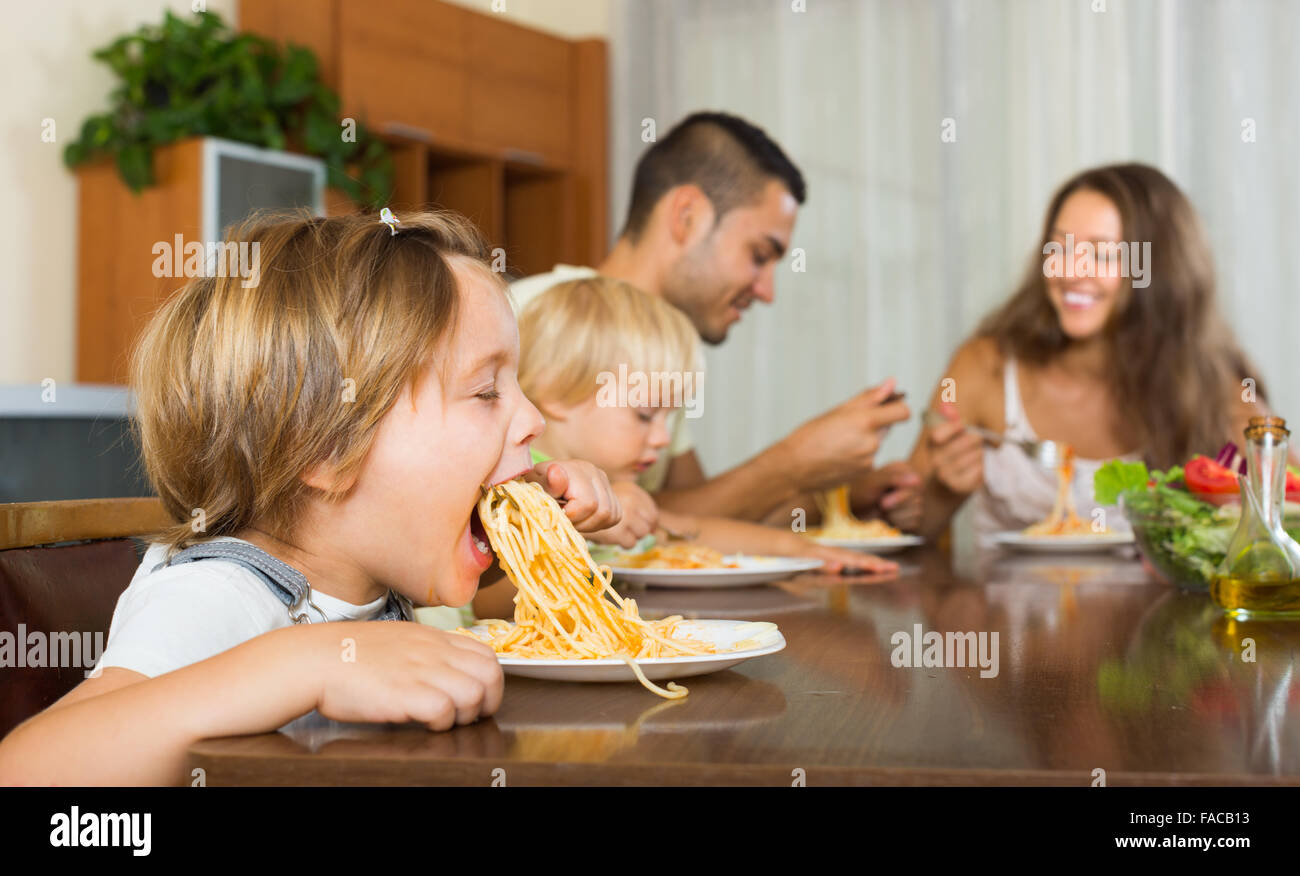 Young family of four eating with spaghetti at table. Focus on girl ...