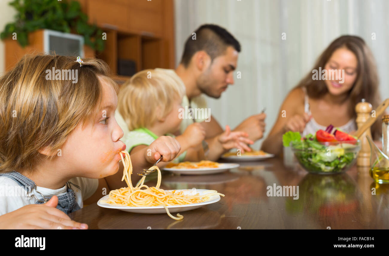 Happy family with playful little daughters eating with spaghetti at ...