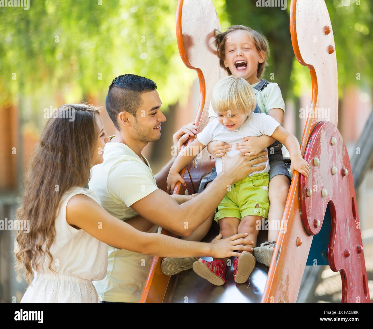 Smiling parents helping two kids on slide in summer day Stock Photo - Alamy