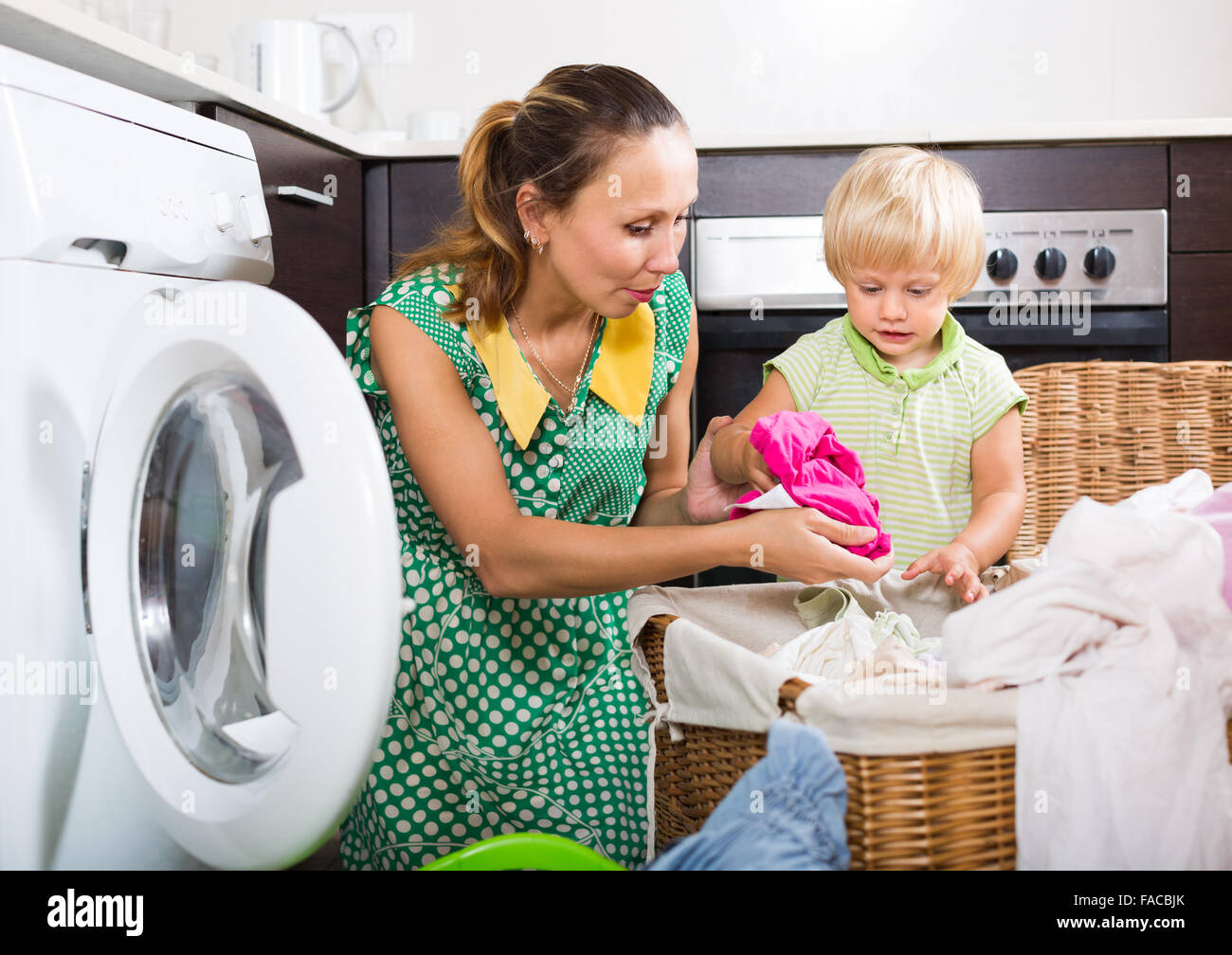 Family laundry. Happy woman with child putting clothes in to washing ...