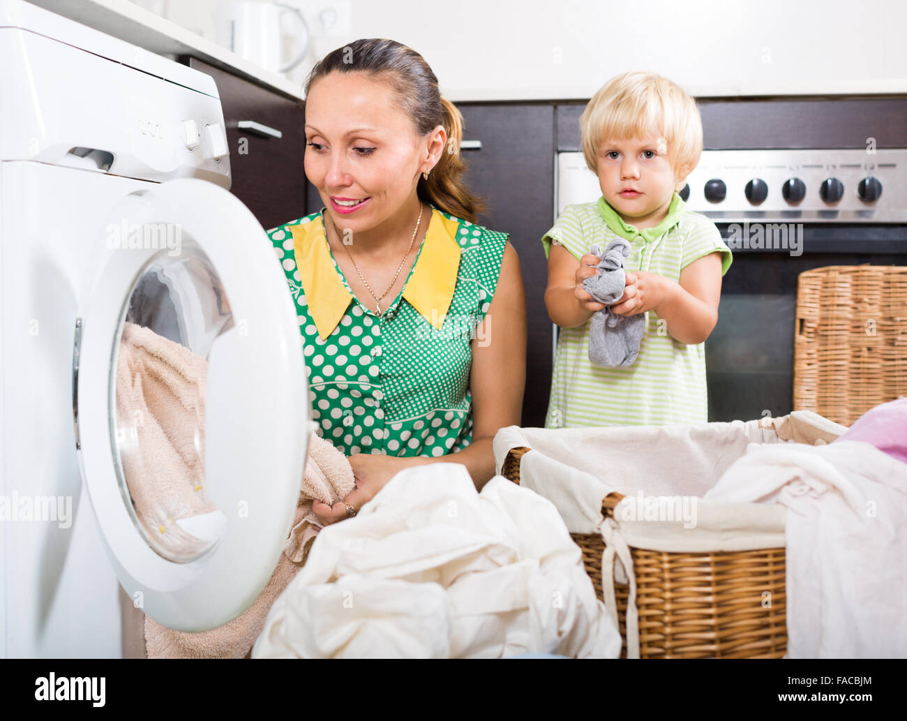Home family laundry. Smiling mother with daughter loading clothes into ...