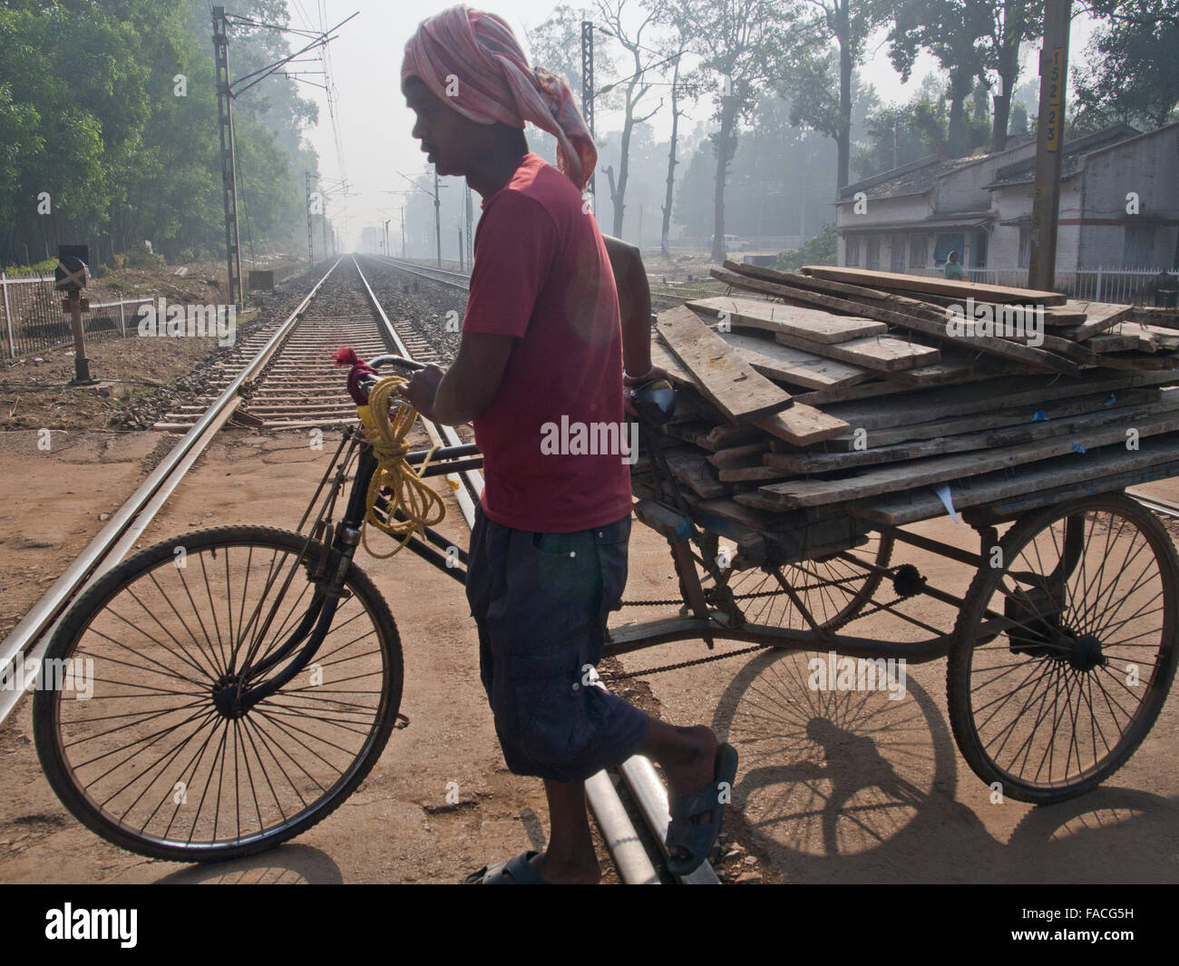 Cyclist carrying timber by railway junction in a town in West Bengal ...