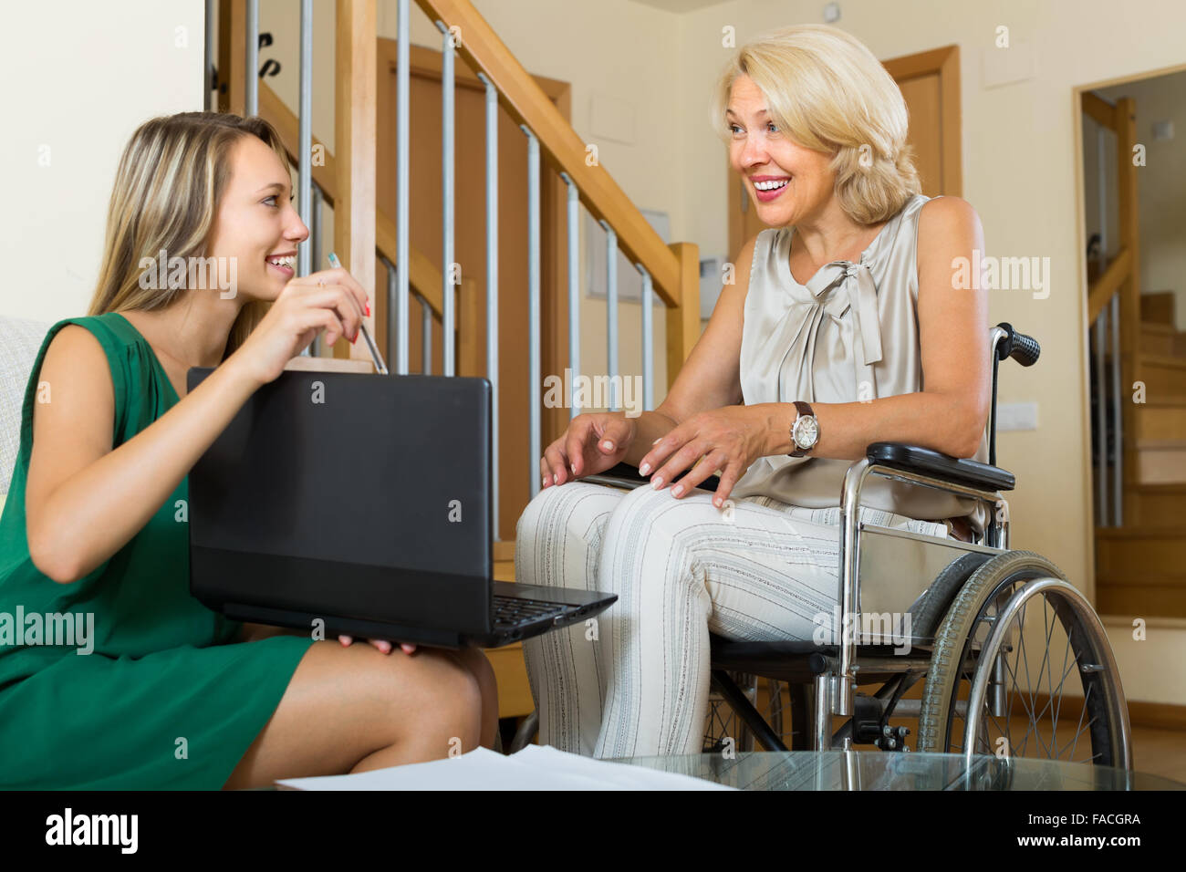 Female social worker with laptop questioning smiling handicapped aged ...
