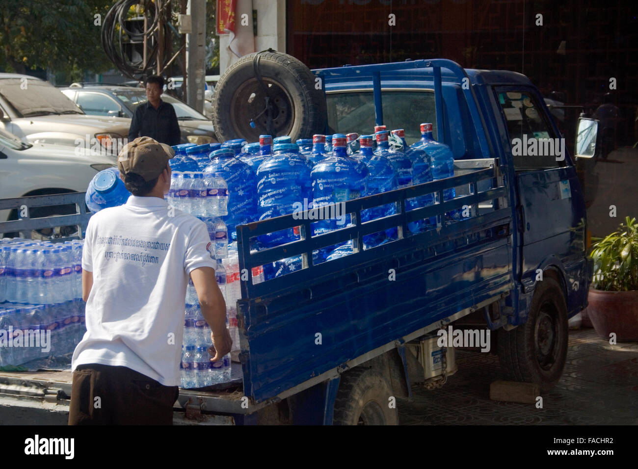 A man is unloading a truck filled with large plastic bottles filled ...