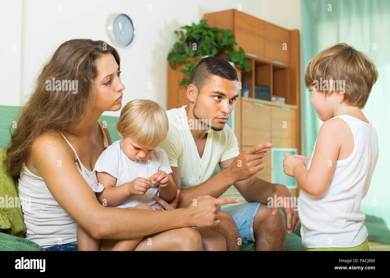 Young parents scolding little child in home interior. Focus on woman ...
