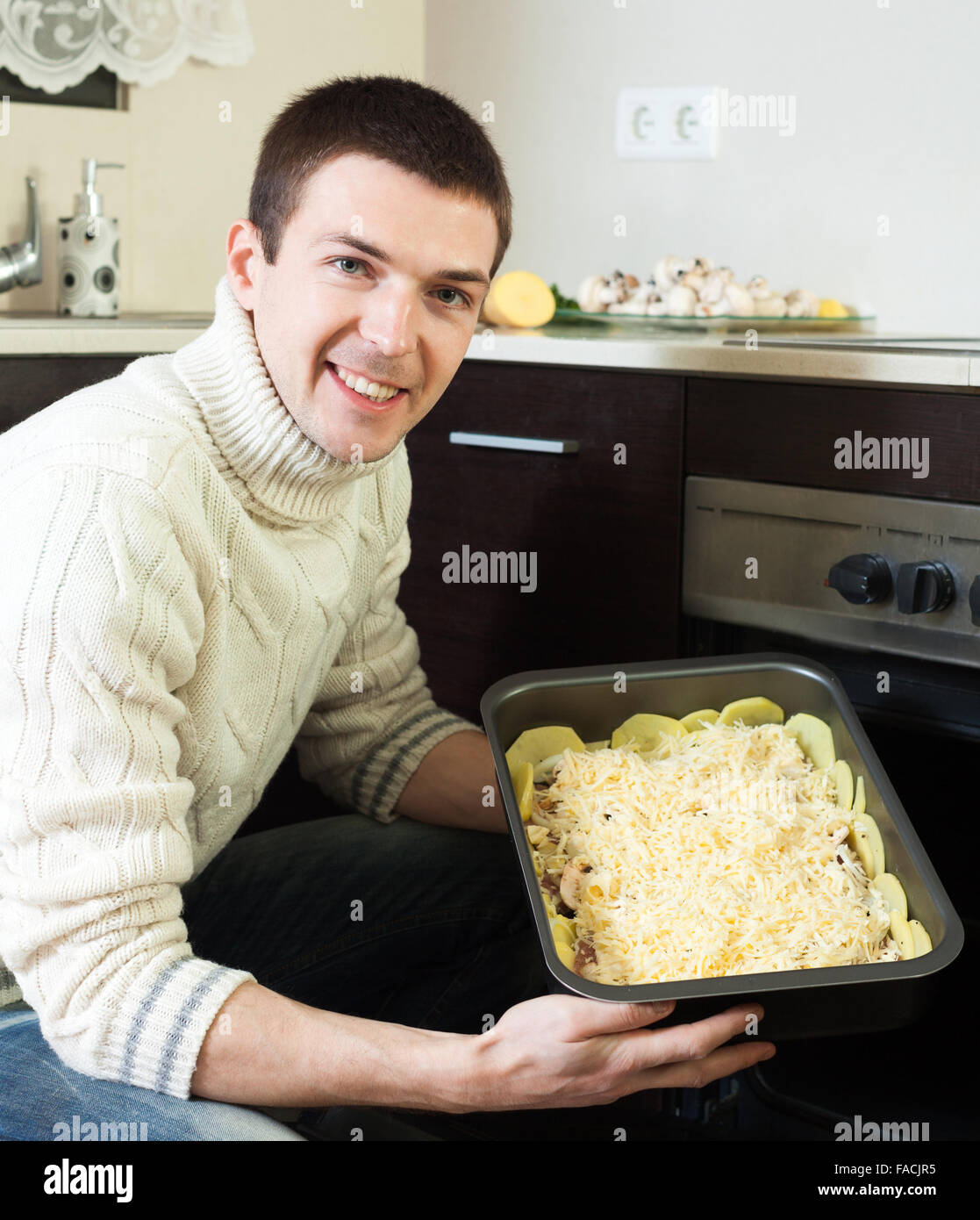 Young happy handsome man cooking french-style meat. Adding grating ...