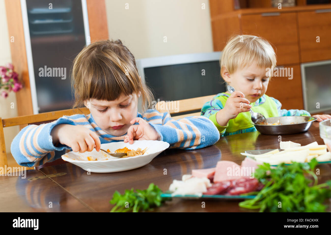 serious children eating food at wooden table in home interior Stock ...