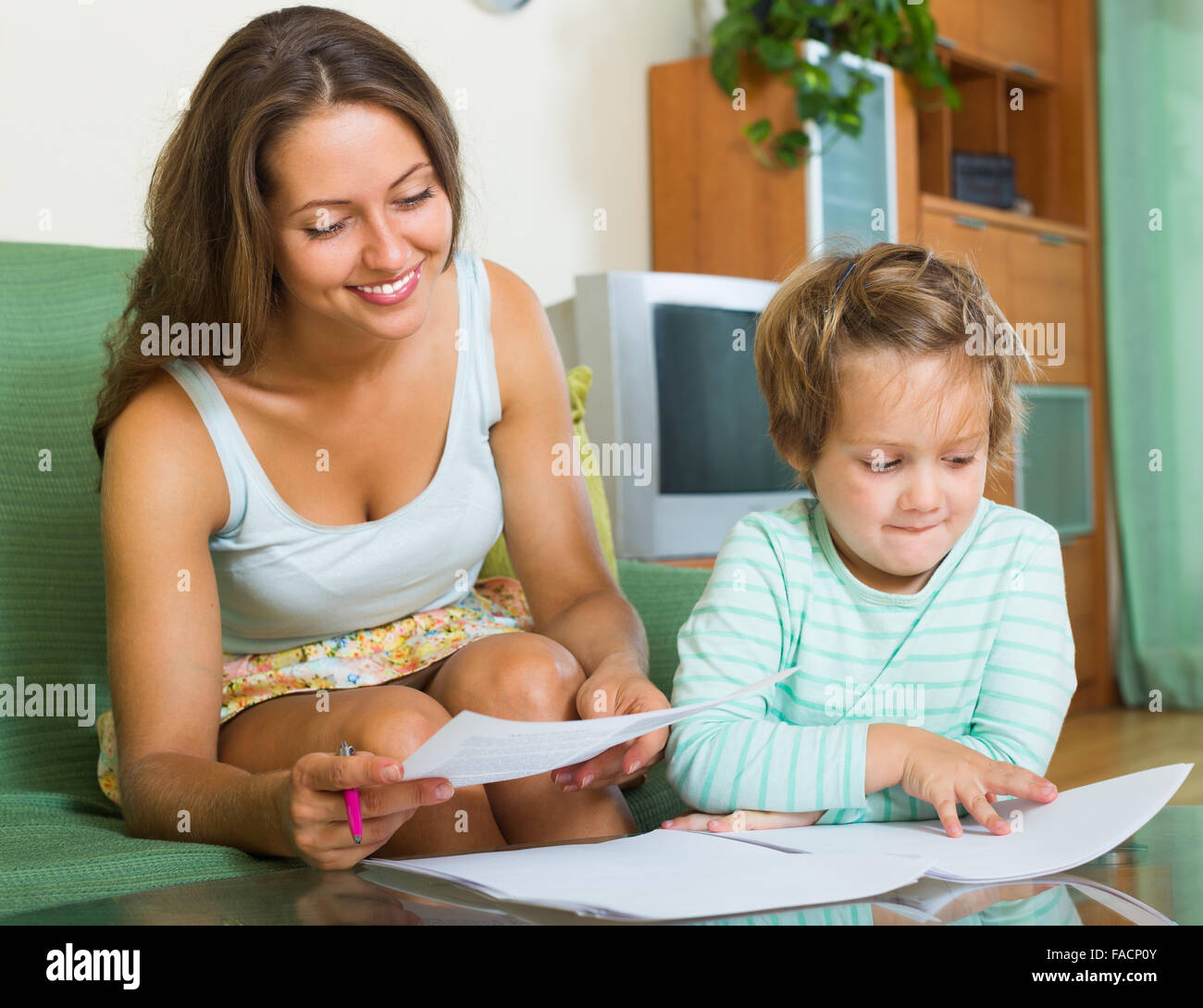 Cheerful woman and daughter signing application form for kindergarten ...
