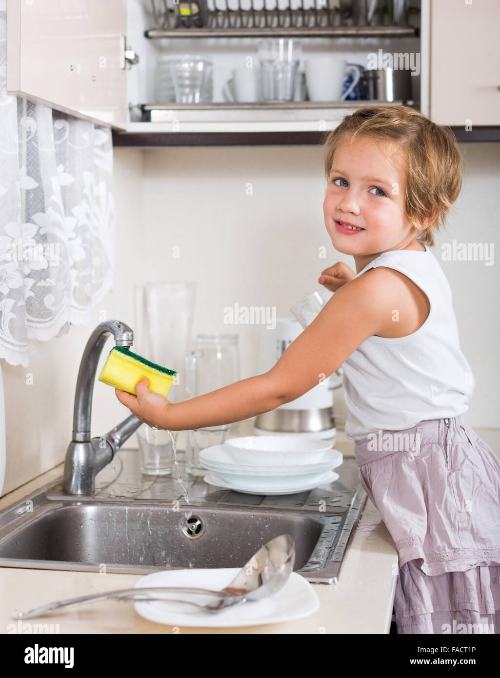 Cute little girl cleaning dishes in the kitchen Stock Photo - Alamy