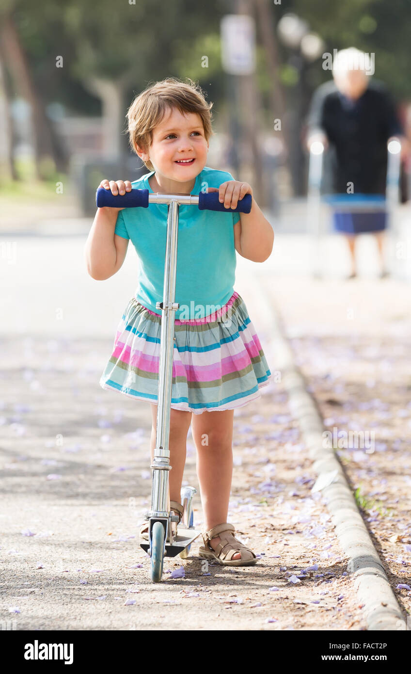 Happy smiling positive little girl riding on scooter in park Stock ...