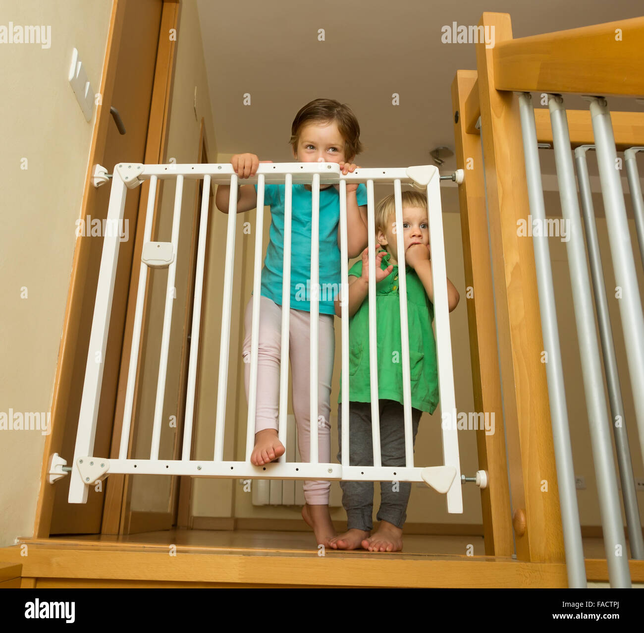 Two little girls approaching safety gate of stairs at home Stock Photo ...