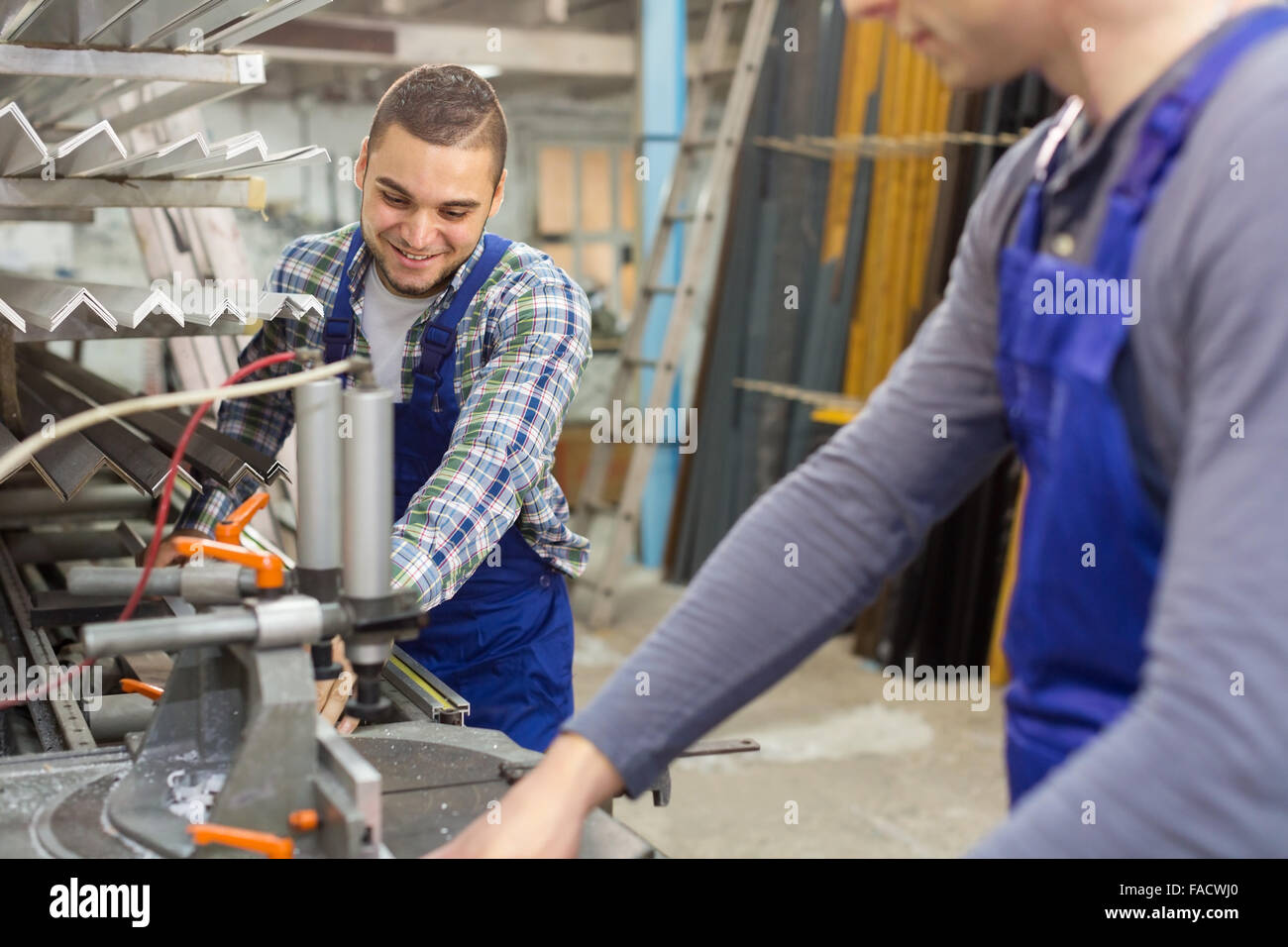 A couple of happy adult workers are working around the milling machine ...