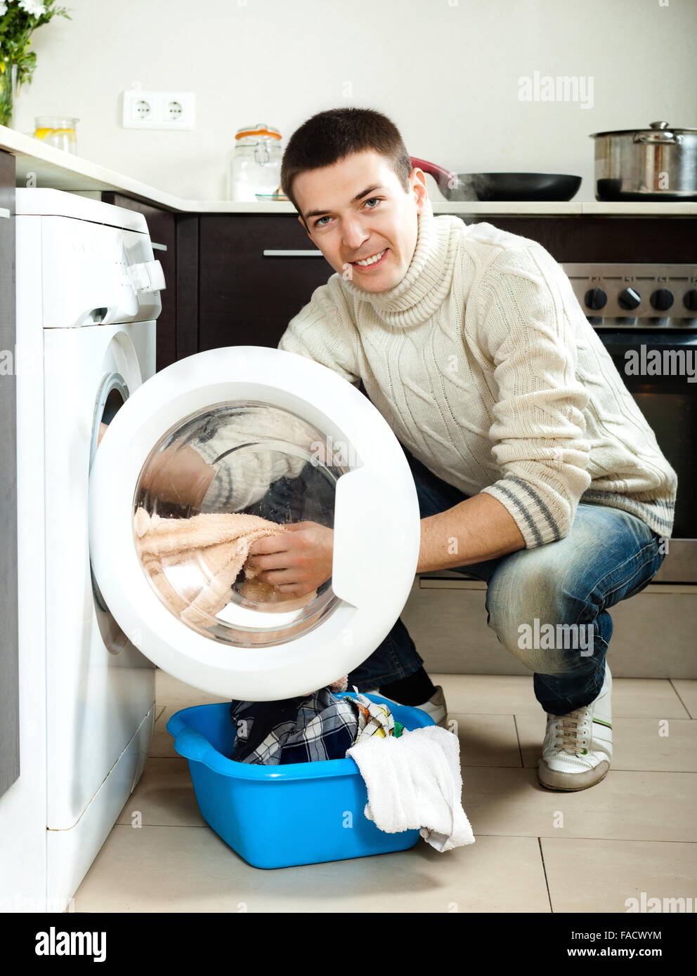 Home laundry. Handsome man loading clothes into the washing machine in ...