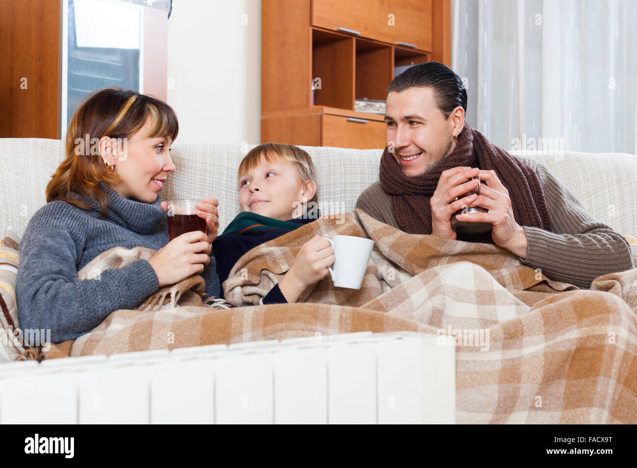 parents and teenage son warming near warm heater in home Stock Photo ...