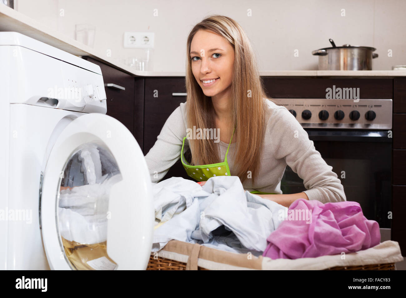Home laundry. Smiling blonde woman putting clothes in to washing ...