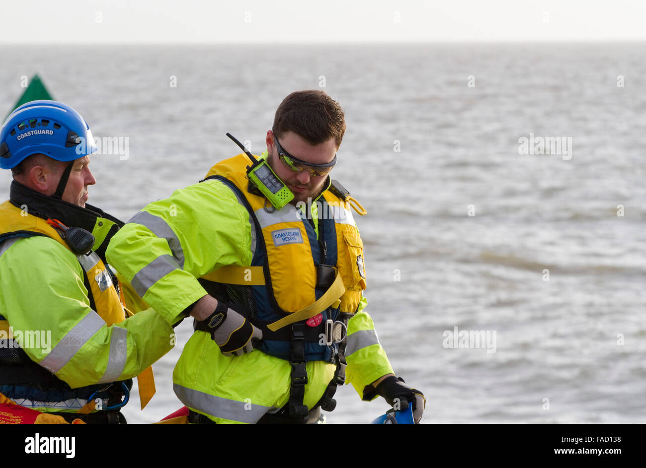 A British coast guard helps a colleague adjust his safety equipment ...