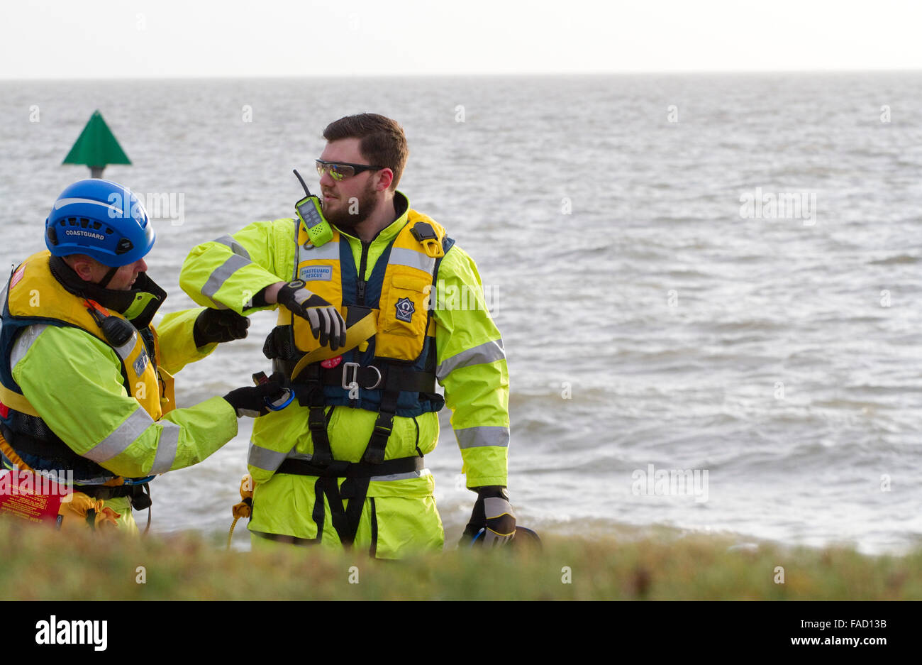 A British coast guard helps a colleague adjust his safety equipment ...