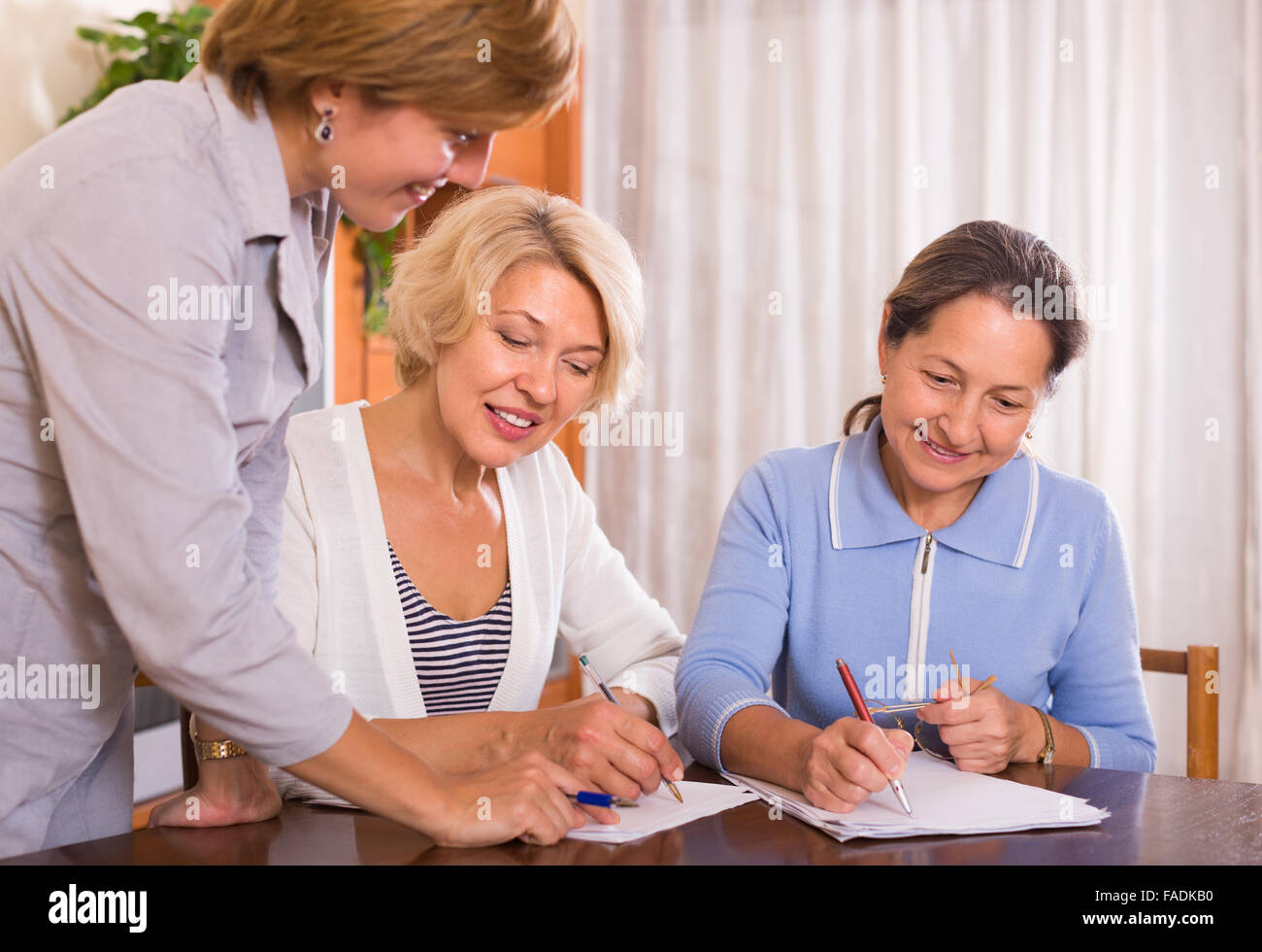 Two senior ladies signing documents at bank and smiling Stock Photo - Alamy