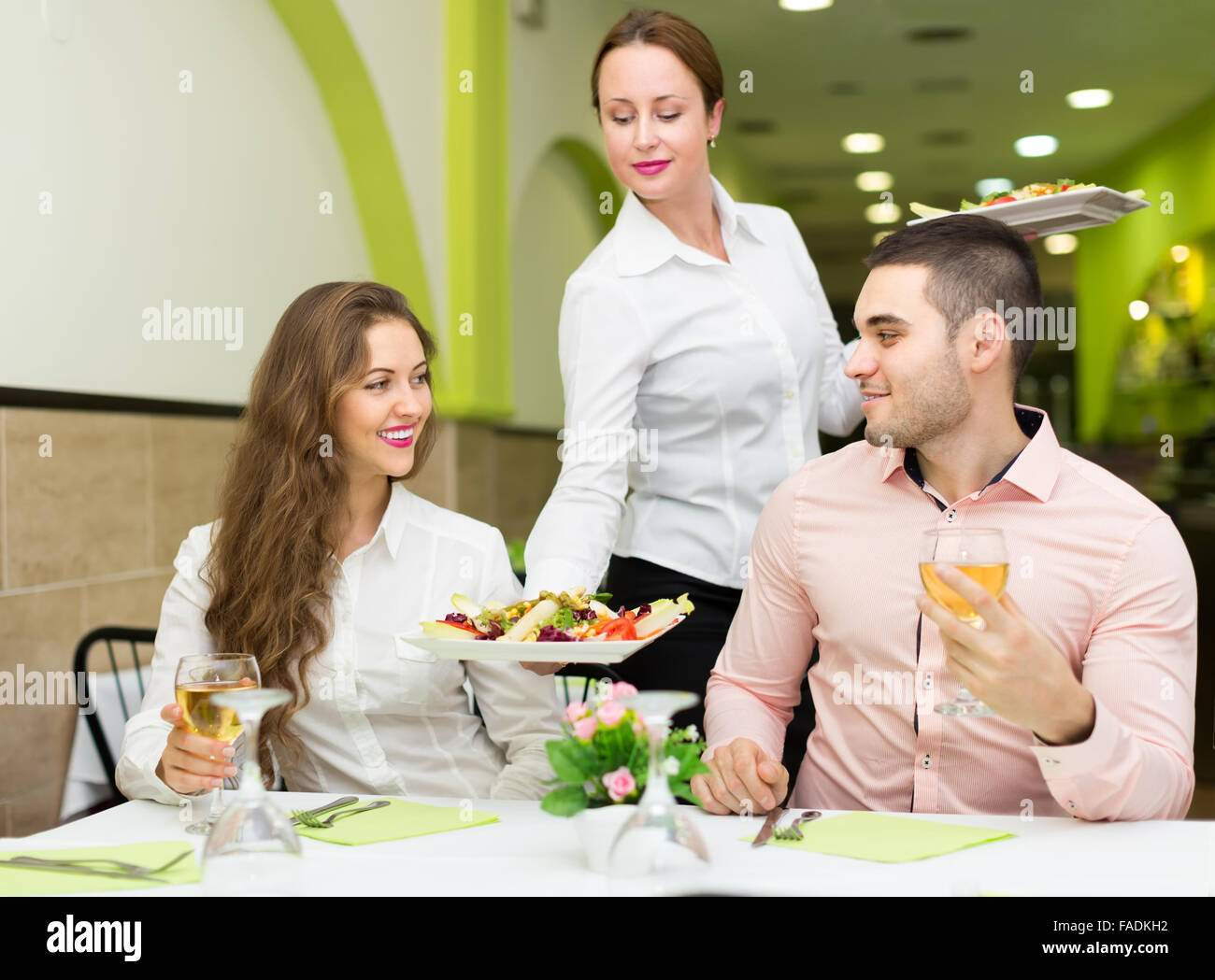 Smiling female waiter with plates serving guests table in cafe. Focus ...