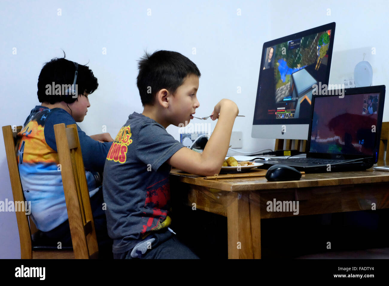young boys sat playing games on computer while eating surrounded by ...